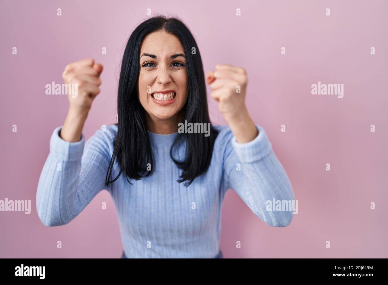 Hispanic woman standing over pink background angry and mad raising ...