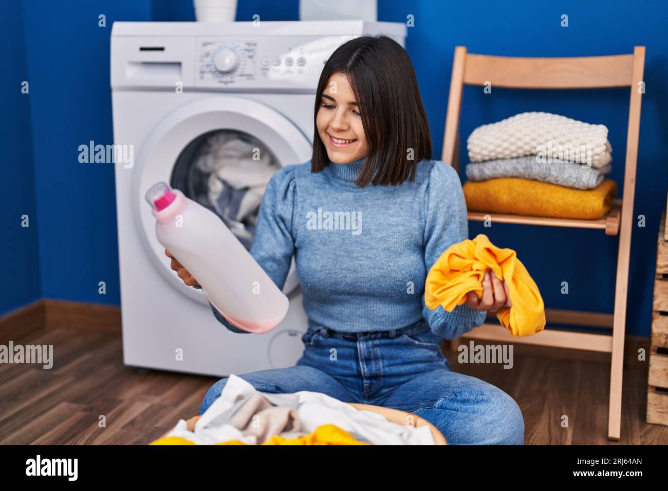 Young beautiful hispanic woman washing clothes holding detergent bottle ...