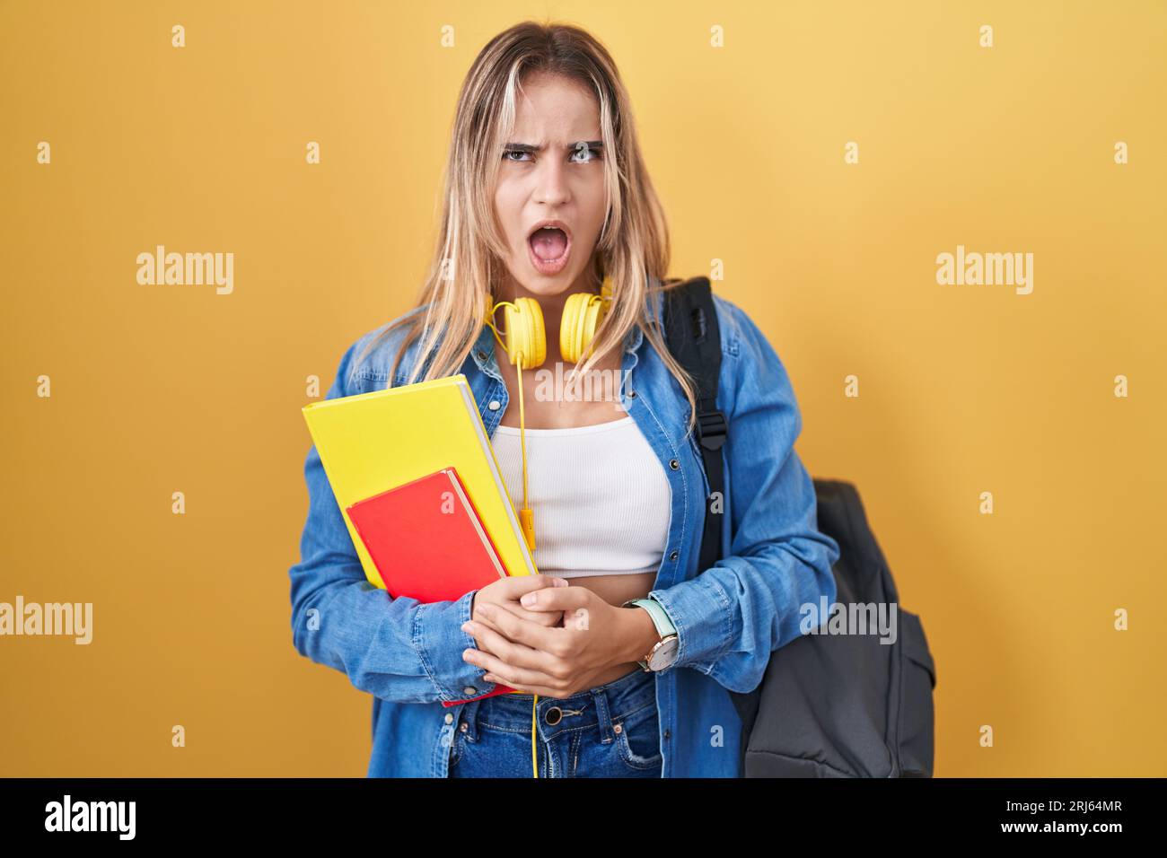 Young blonde woman wearing student backpack and holding books angry and ...
