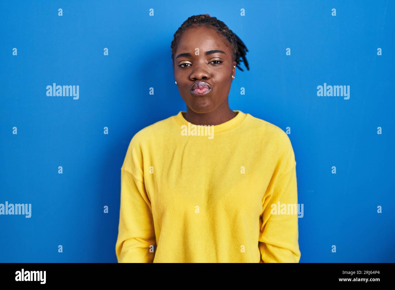 Beautiful black woman standing over blue background puffing cheeks with ...
