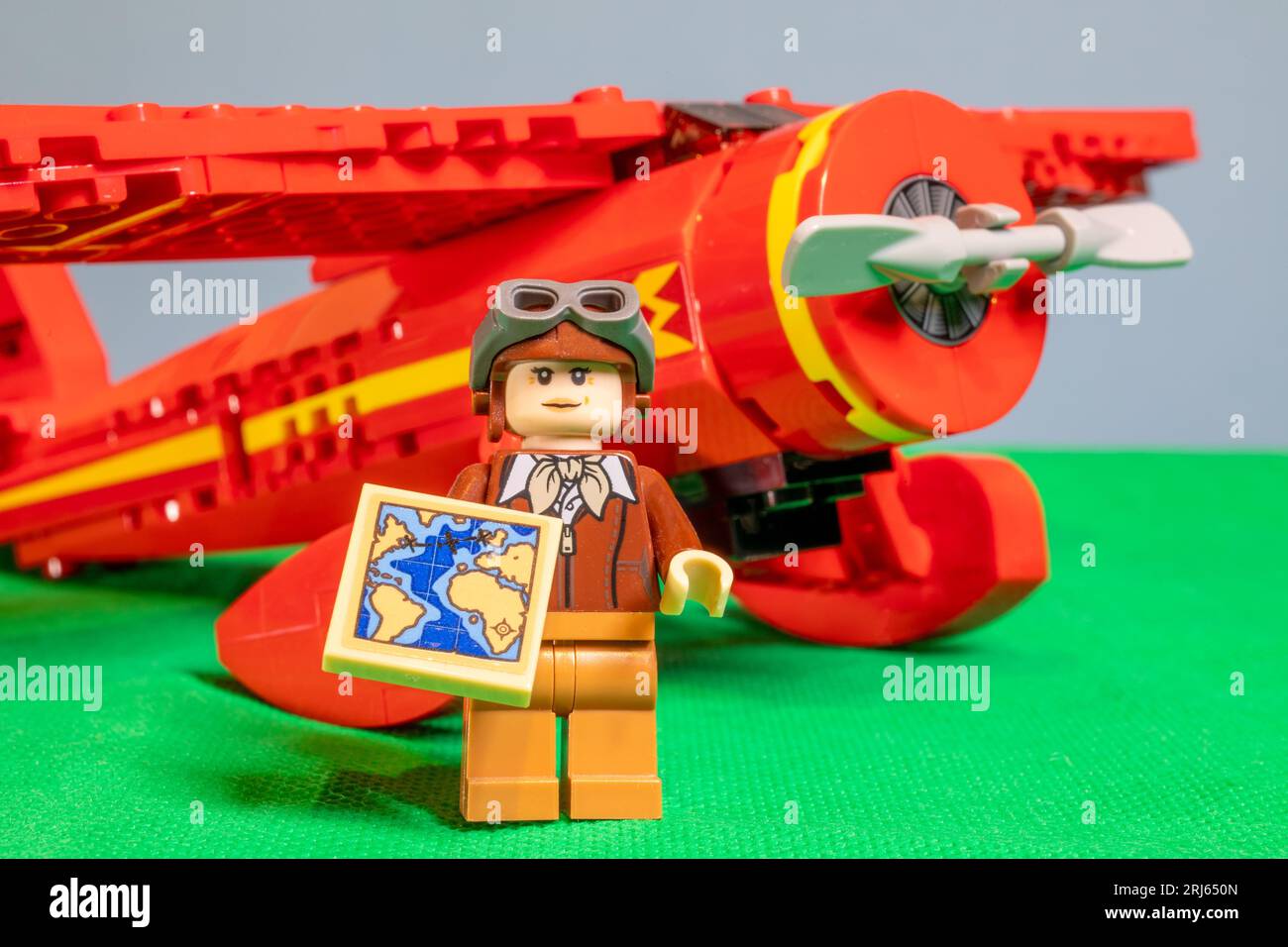 A Lego figure stands alongside a toy plane on the lush green background ...