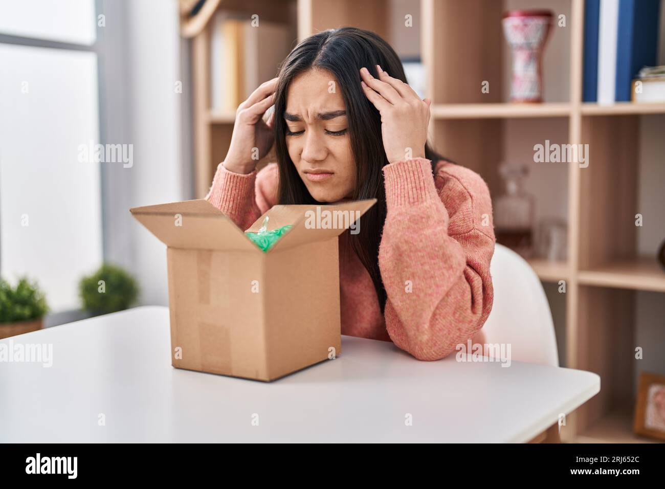 Young south asian woman opening cardboard box with hand on head ...