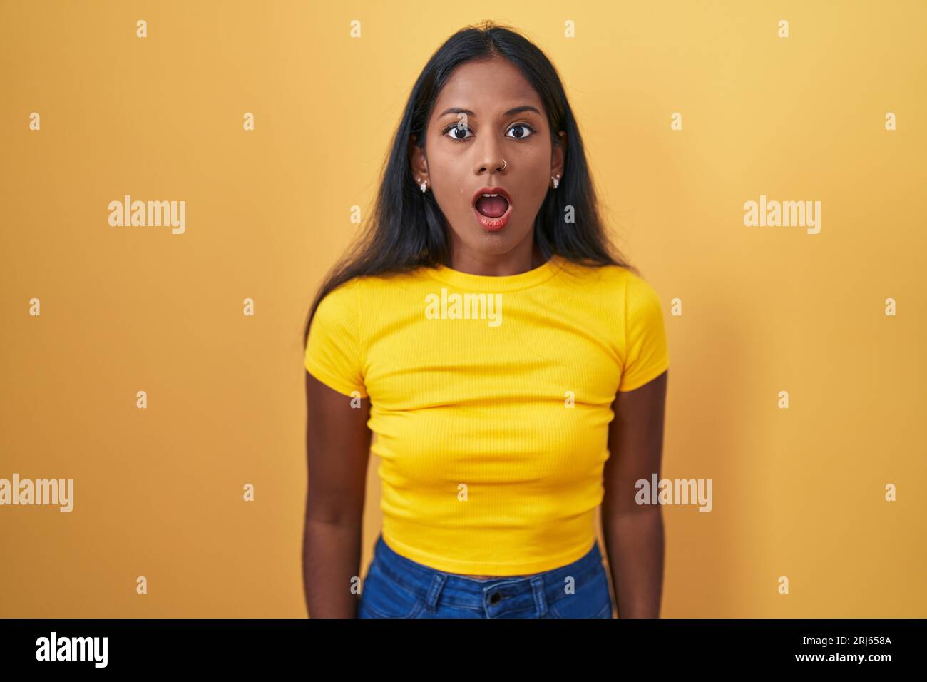 Young indian woman standing over yellow background afraid and shocked ...