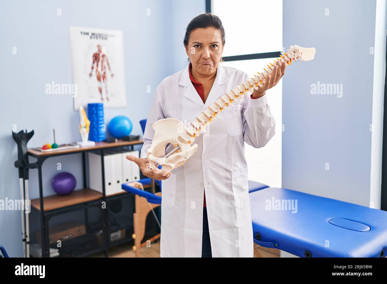 Middle age hispanic woman holding anatomical model of spinal column ...