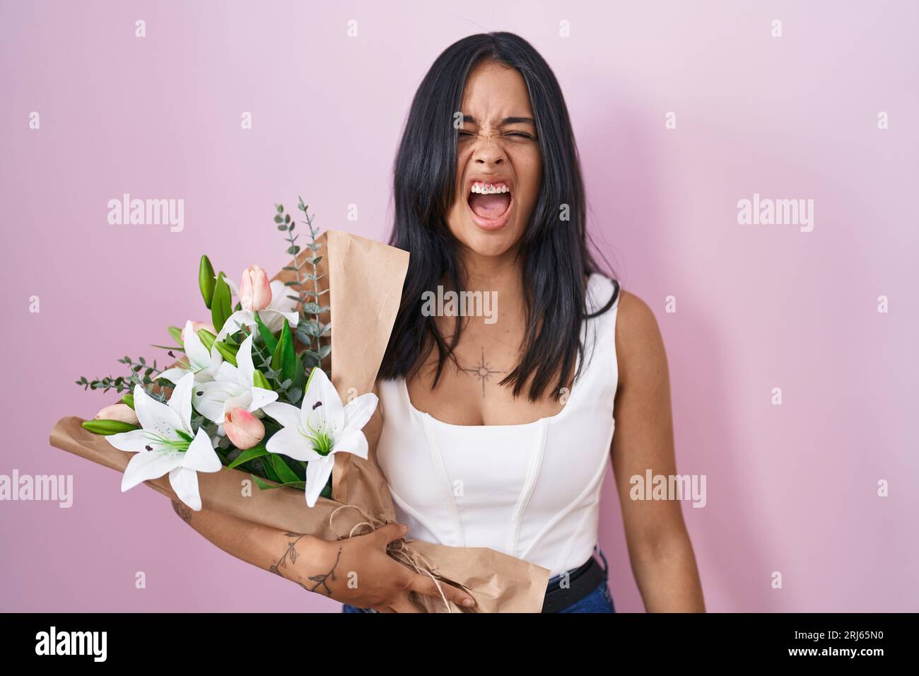 Brunette woman holding bouquet of white flowers angry and mad screaming ...