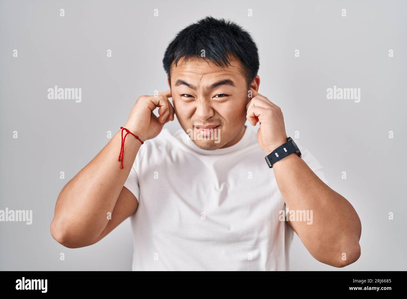 Young chinese man standing over white background covering ears with ...