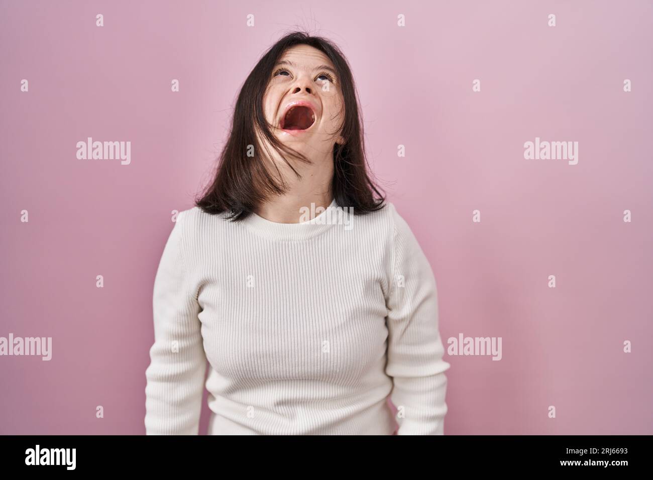 Woman with down syndrome standing over pink background angry and mad ...