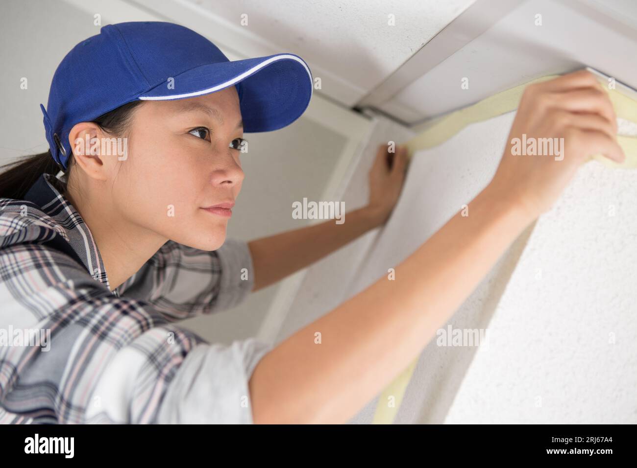 woman painter worker protecting ceiling moulding with masking tape ...
