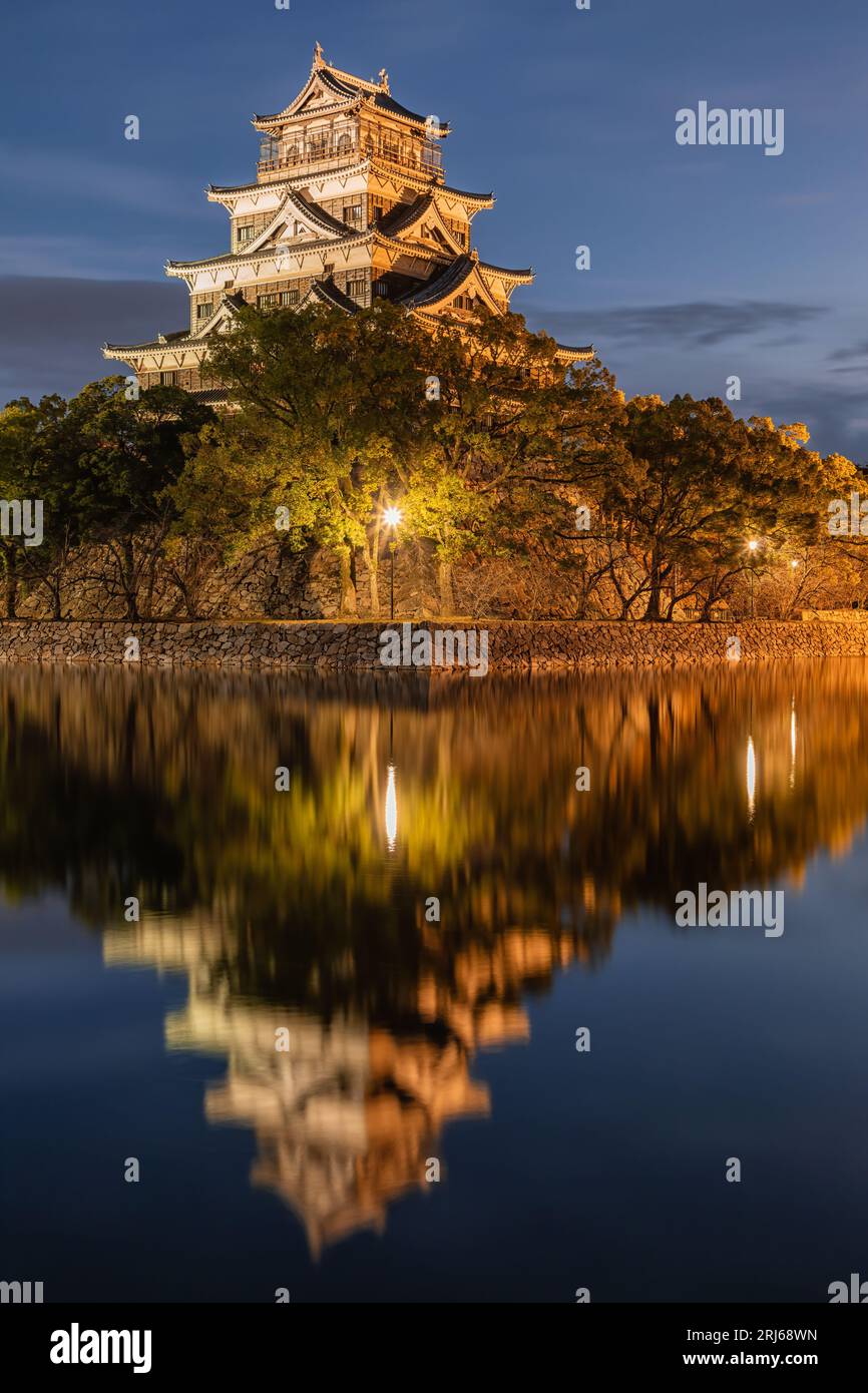Hiroshima castle in Japan lit up at night time and reflecting in the ...