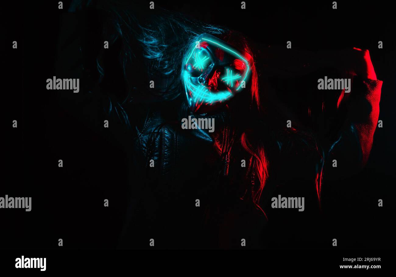 A crazy girl in an ominous neon mask striking a pose in a dark room ...