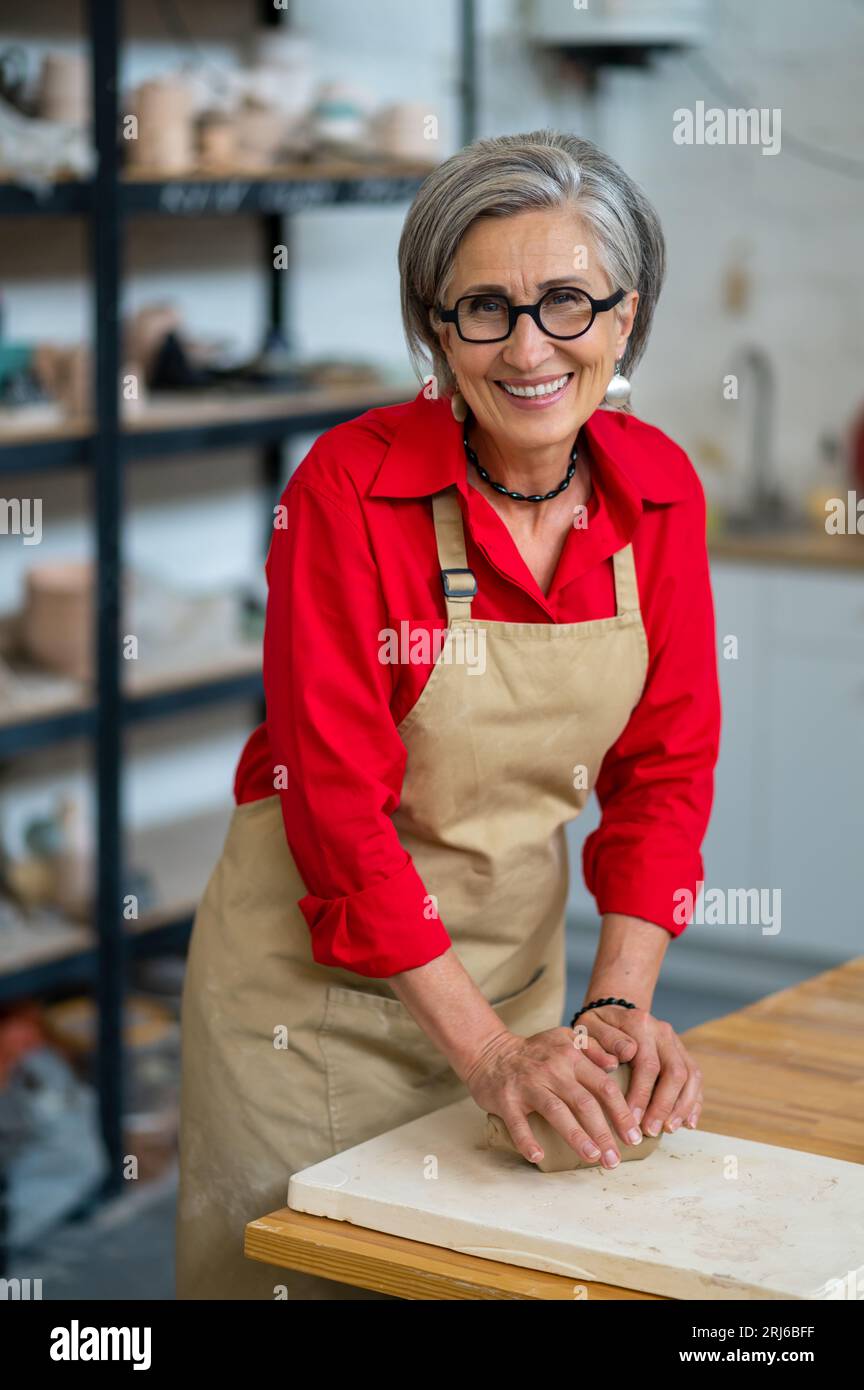 Mature woman wedging clay with hands standing behind table in studio ...