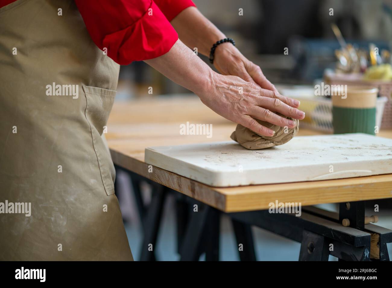 Unrecognizable woman wedging clay with hands standing behind table in ...