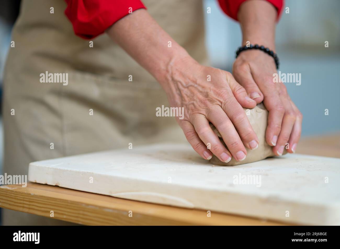 Unrecognizable woman wedging clay with hands standing behind table in ...