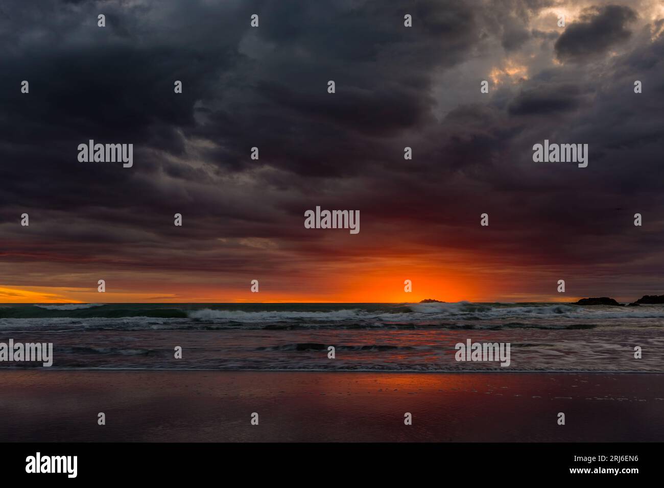 Breaking waves and thick dark clouds glow as the sun sets into the ...