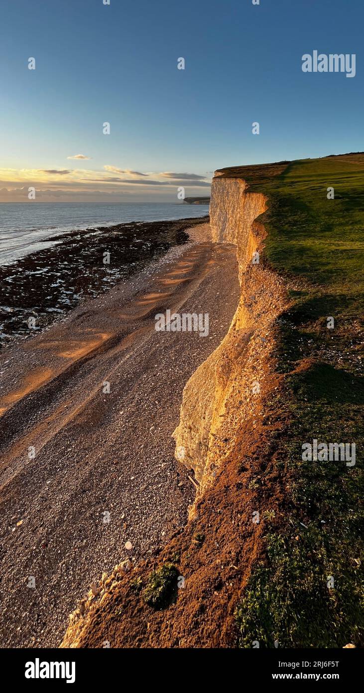 A scenic view of the ocean along a cliff edge at sunset, illuminated by ...