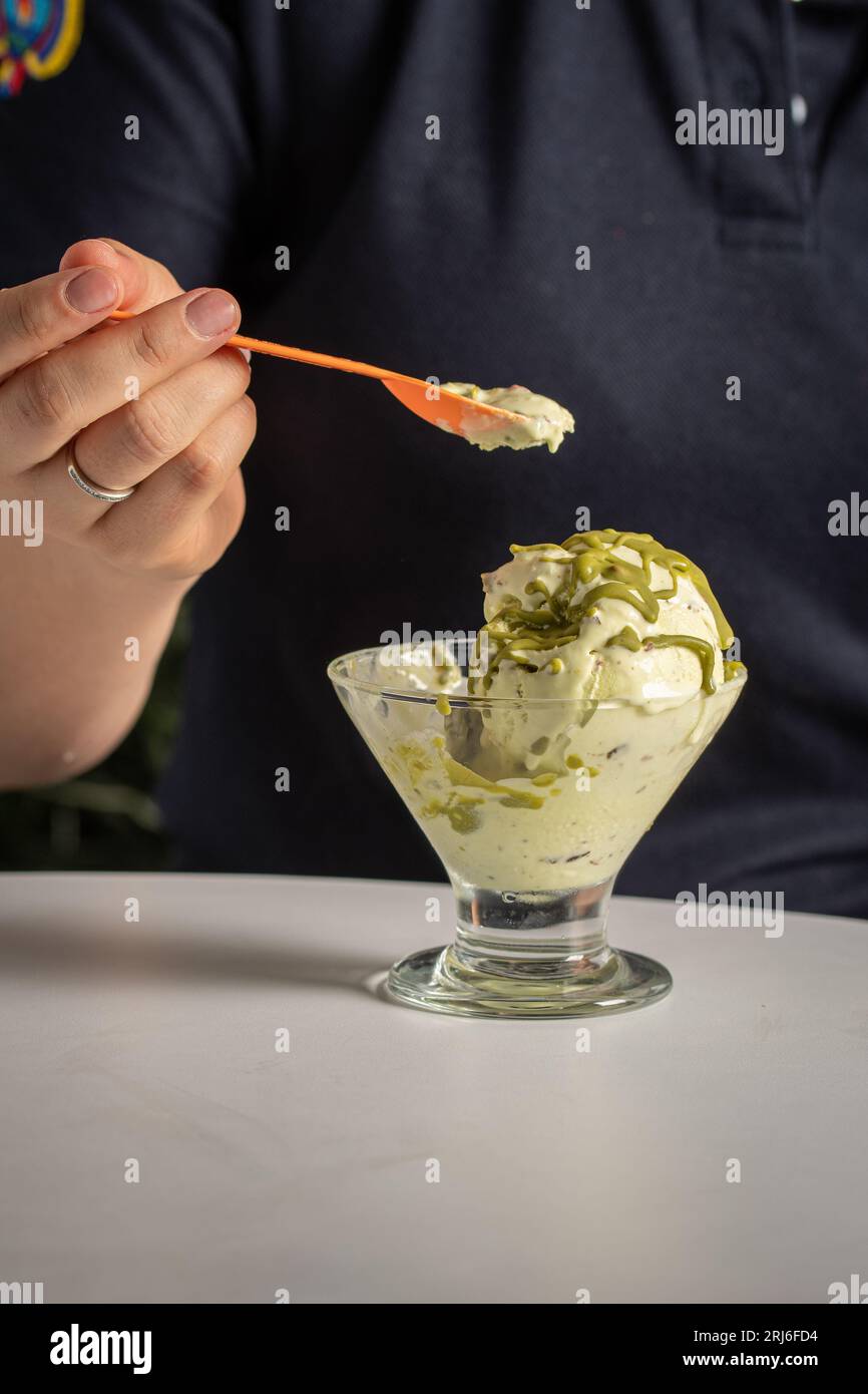 A person eating a delicious ice cream topped with green pistachio Stock ...
