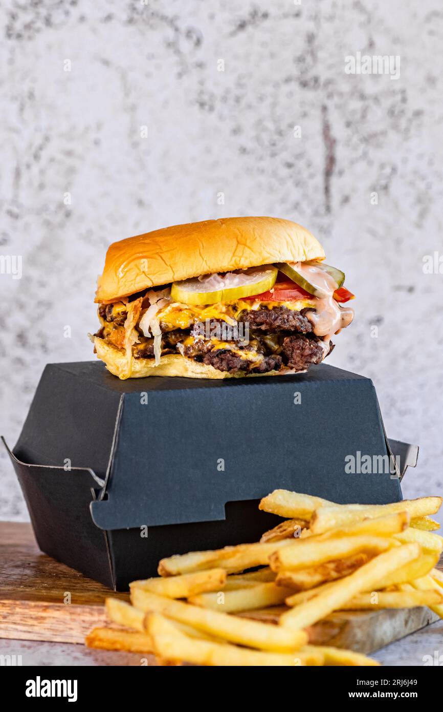 A closeup of a smash burger with cheese, pickles, tomatoes, ranch ...