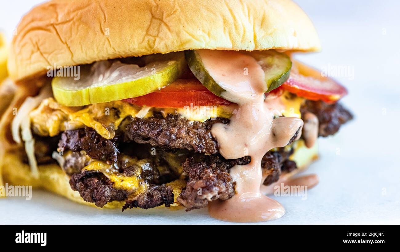 A closeup of a smash burger with cheese, pickles, tomatoes, ranch ...