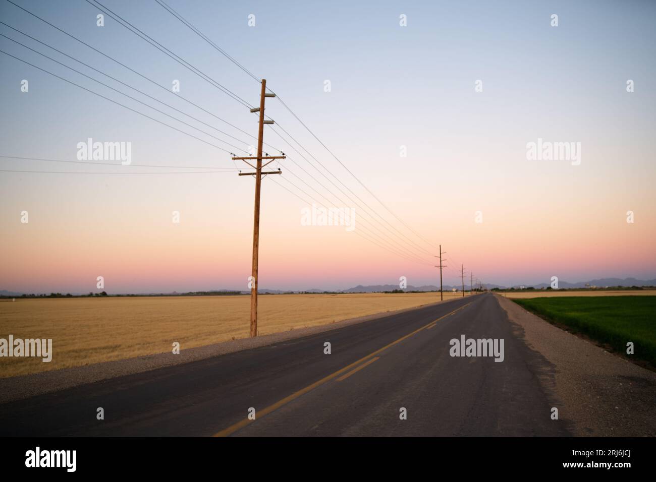 An empty rural road with power lines at sunset Stock Photo - Alamy