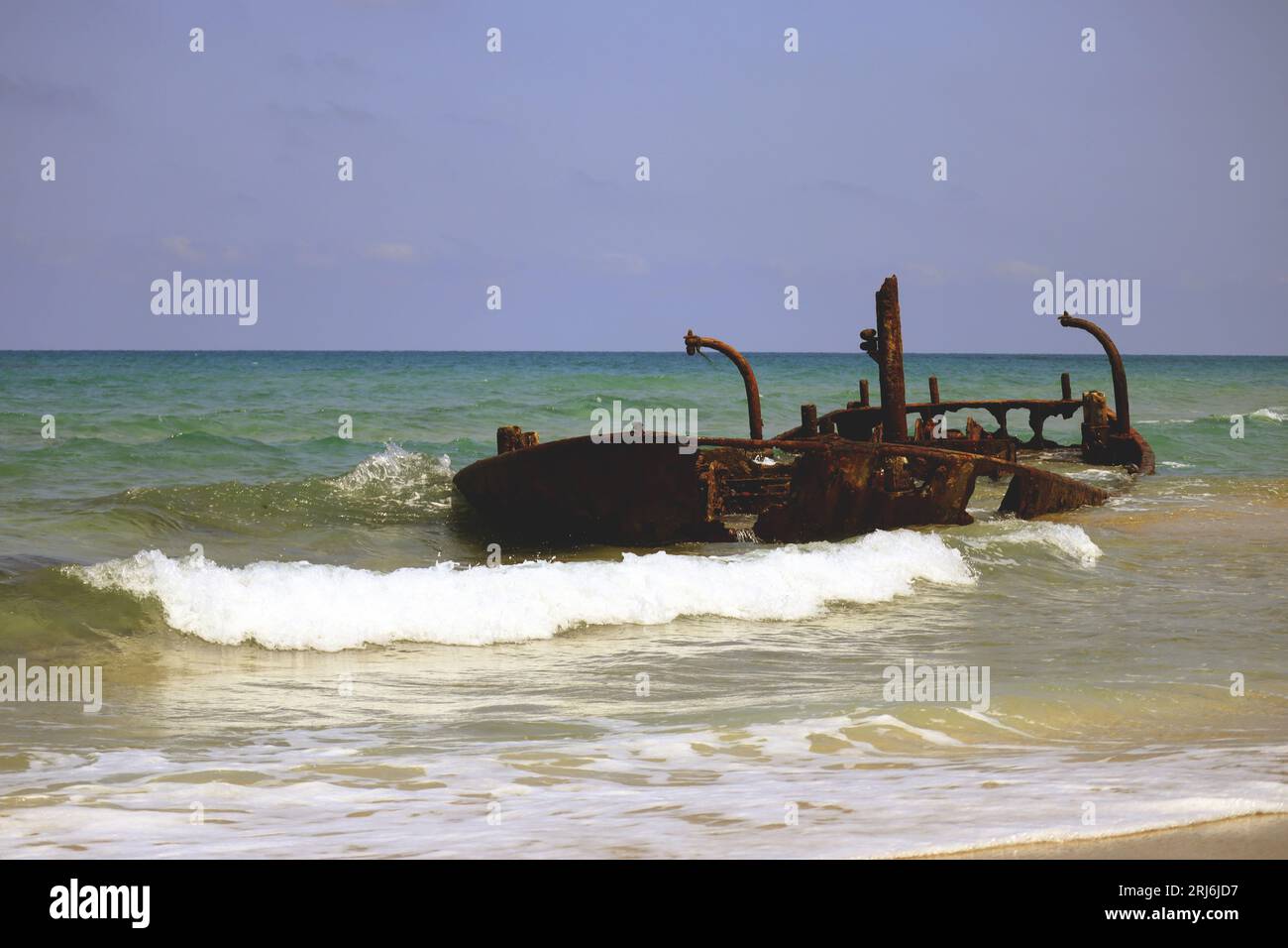 An old rusty boat was washed up on a sandy beach. The sea waves ...