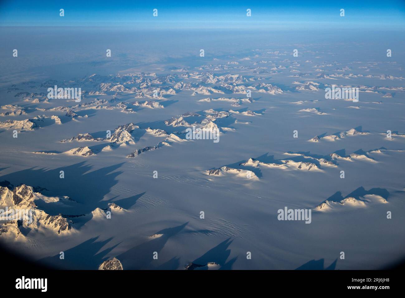 An aerial view of a vast, snow-covered mountain range, visible through ...