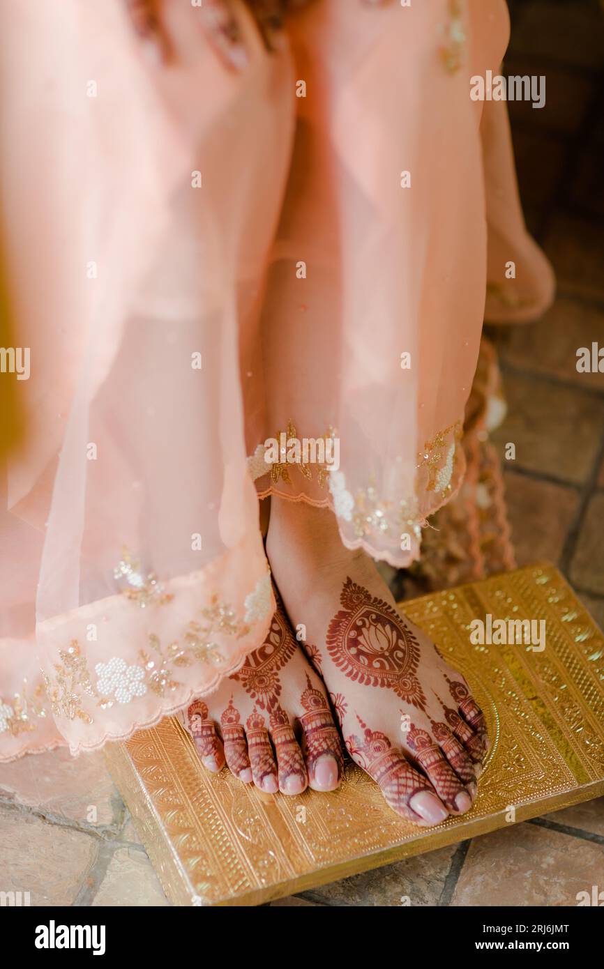A close-up shot of an Indian bride's feet with henna standing atop a ...