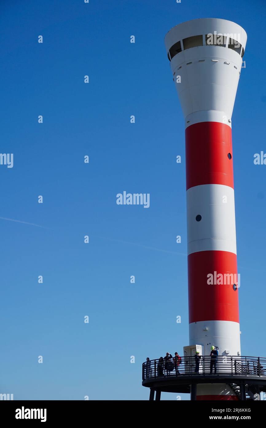 People on the platform of a red-white lighthouse in front of blue sky ...