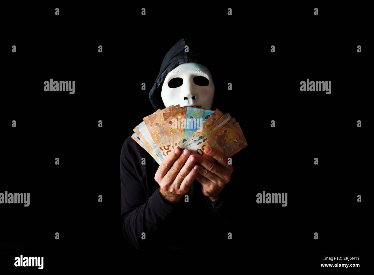 hacker man dressed in black with white mask and black hood holding euro ...