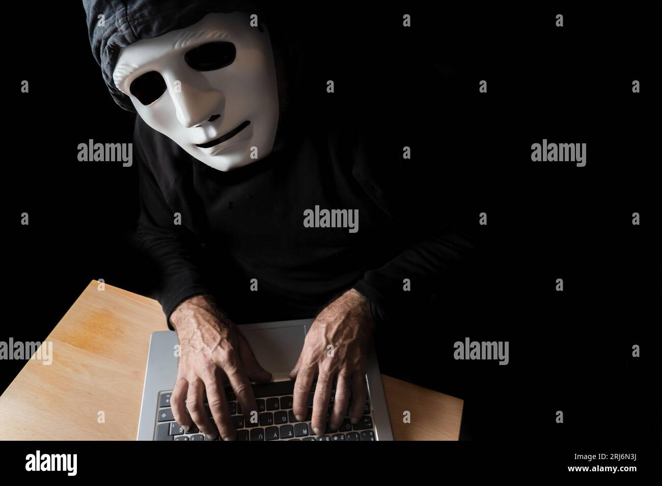 hacker dressed in black with mask and hood typing on a computer while ...