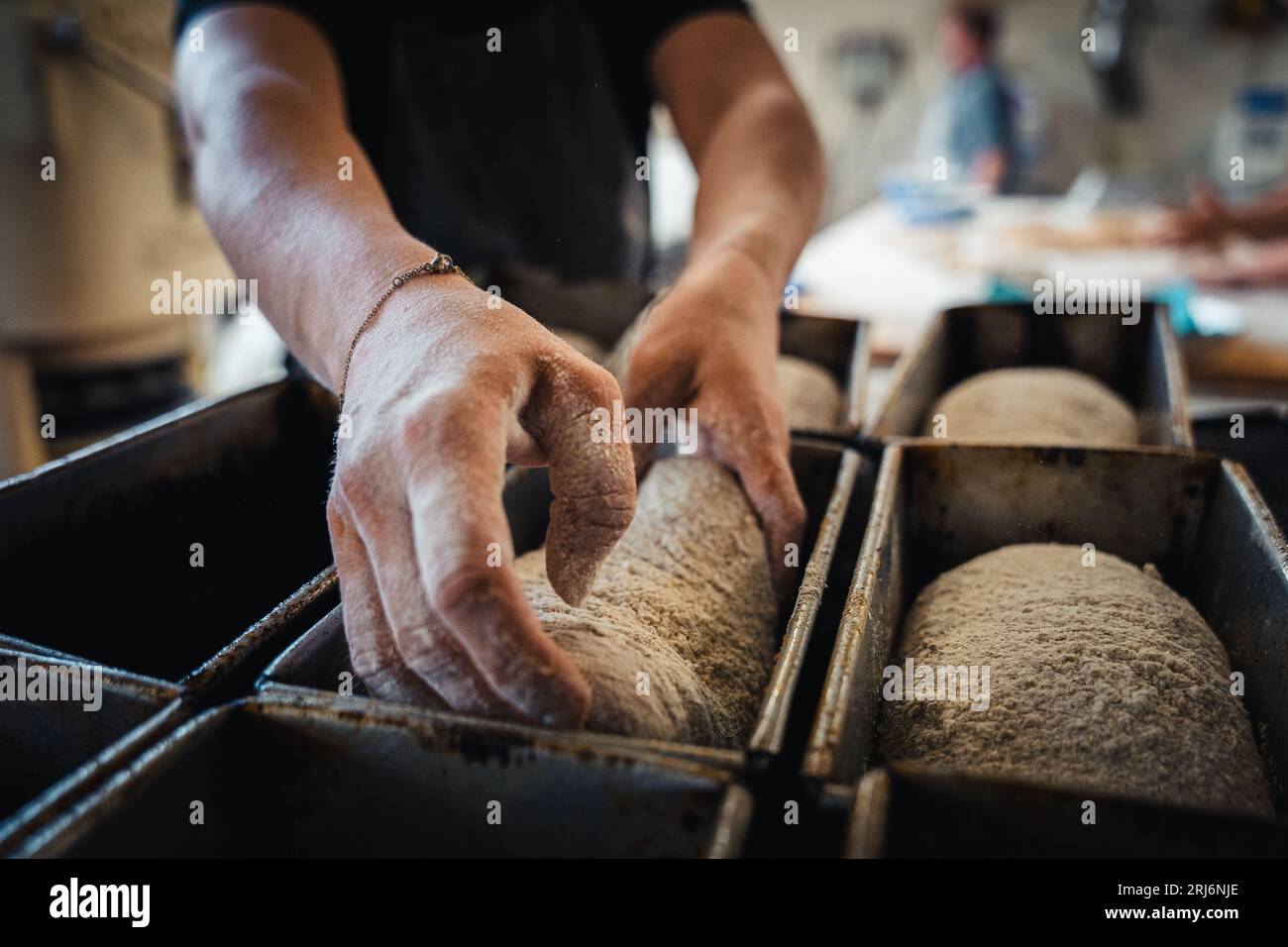 A male baker can be seen inserting freshly made dough into a stainless ...