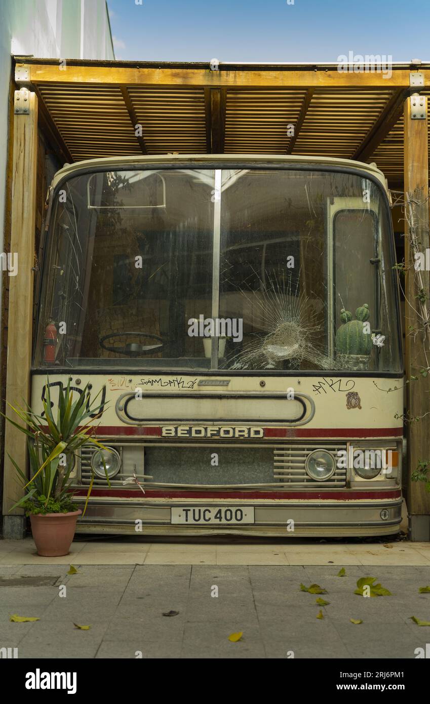 A vintage-looking white bus parked in front of a building with a broken ...