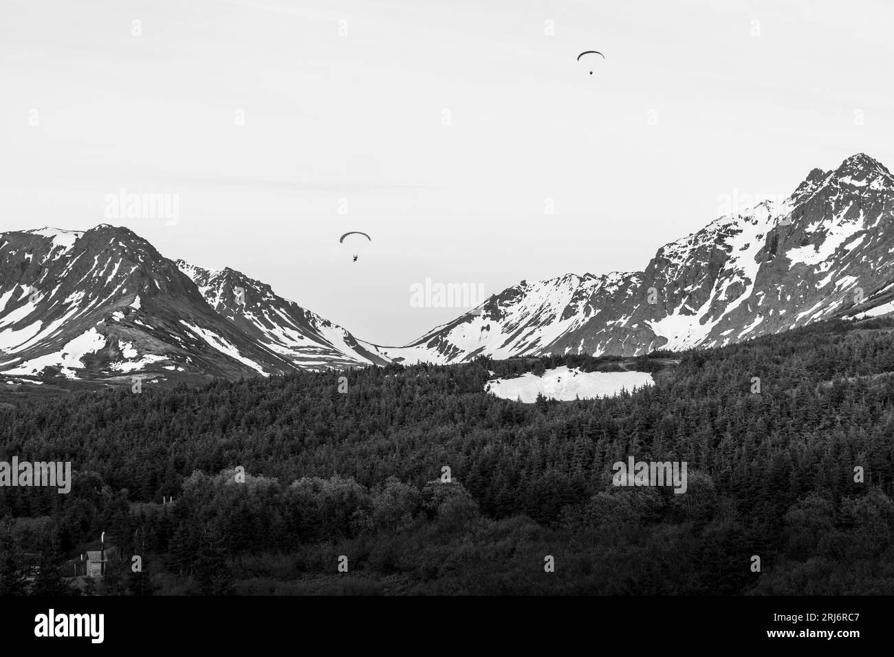 A grayscale of men paragliding, his parachute billowing in the wind ...