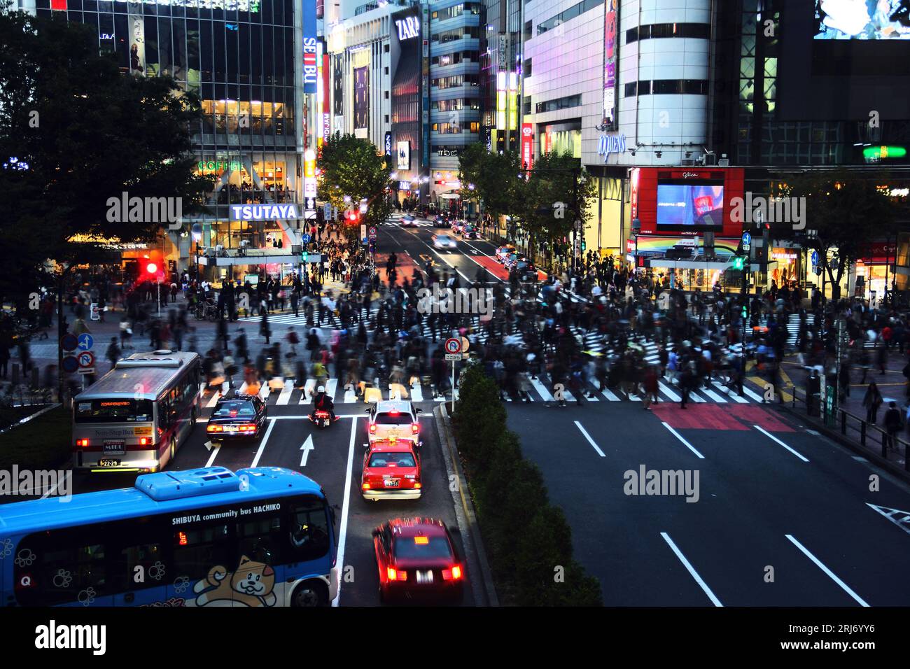 A bustling intersection in Tokyo, Japan, featuring cars, pedestrians, and buildings illuminated ...