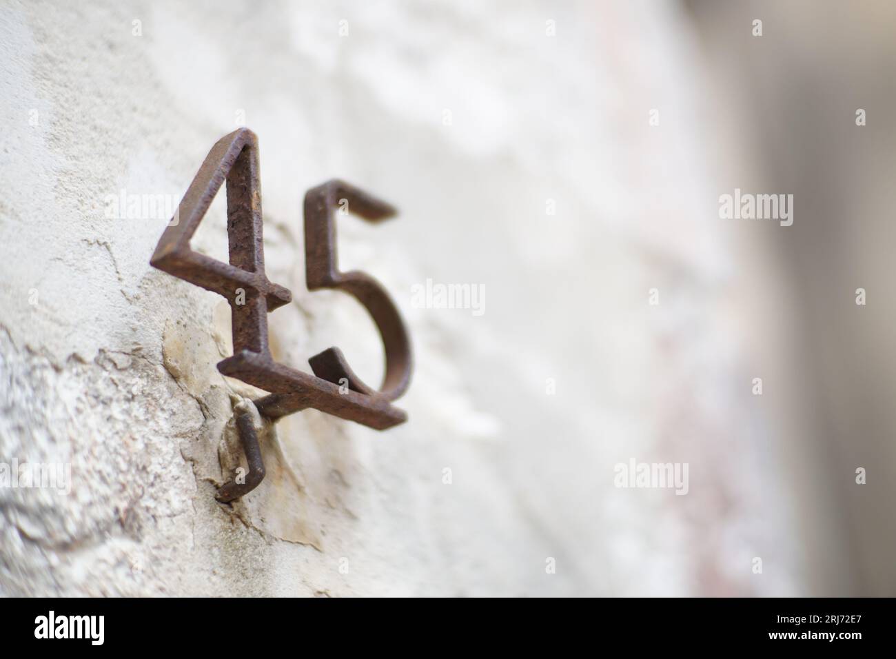 A rusted metal hook is affixed to the side of a wall, with the number ...