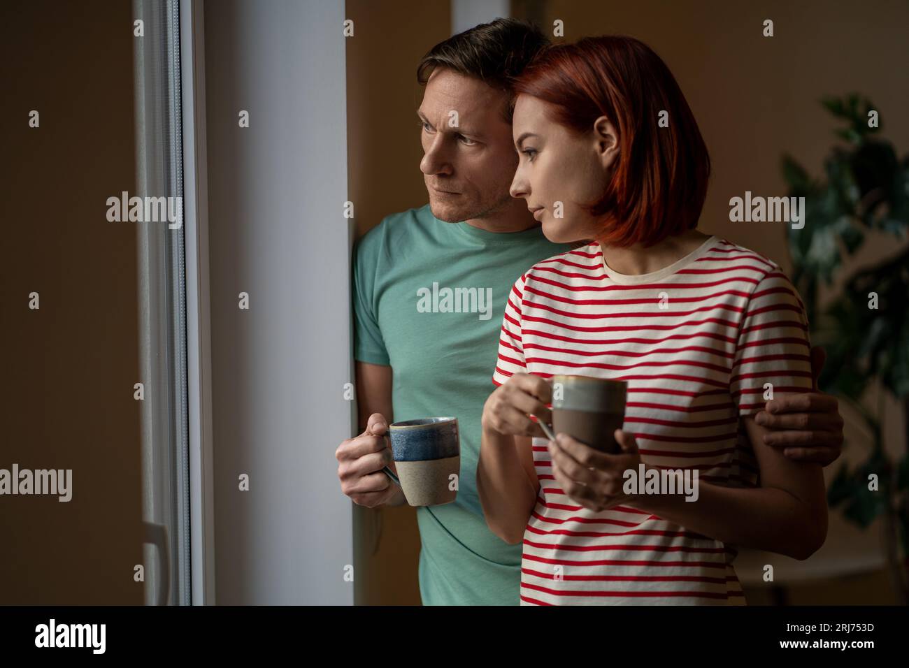 Man and woman with mugs of coffee look out window. Reluctance to leave ...