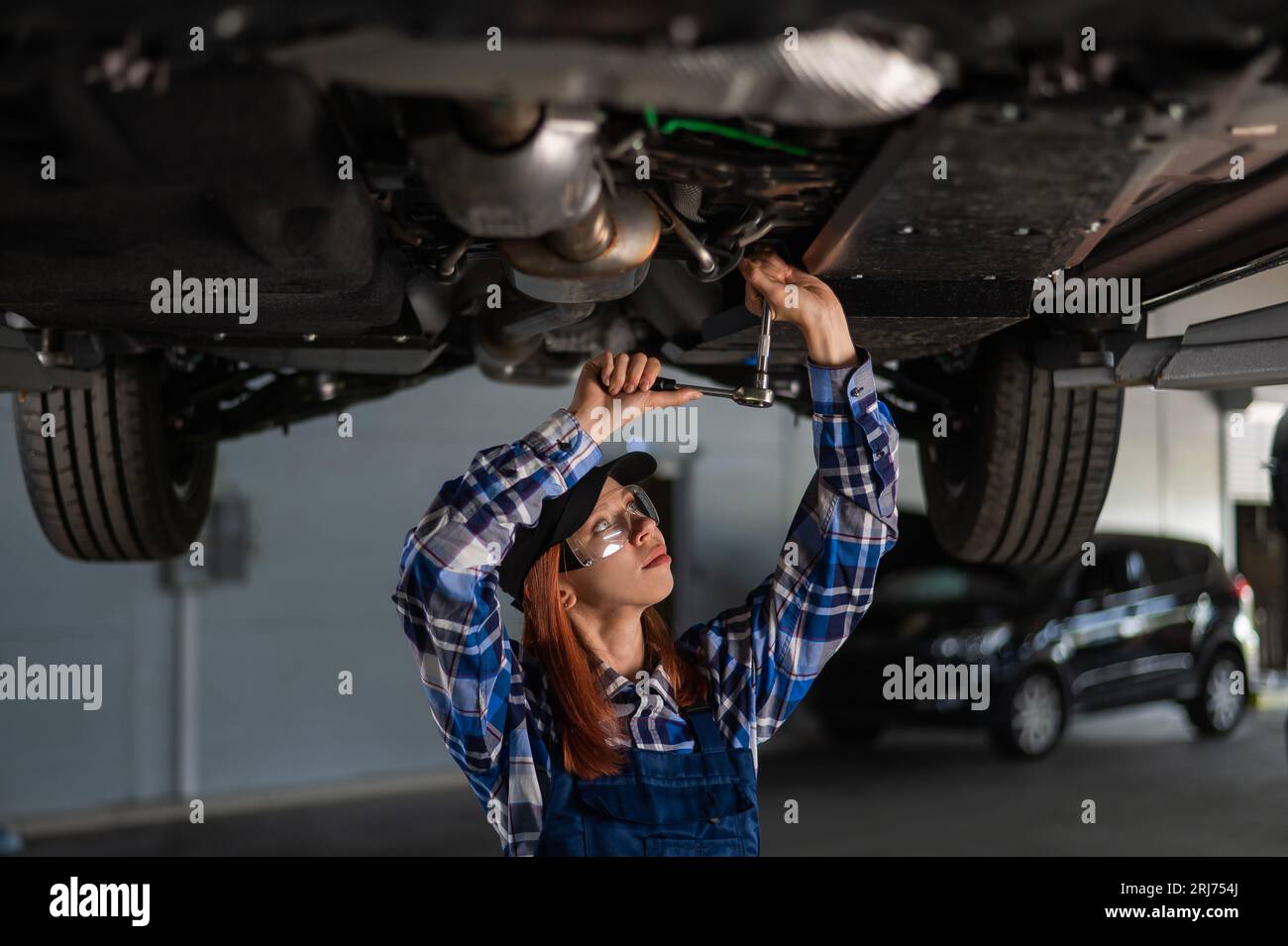 Female mechanic unscrew the nuts on the bottom of the car that is on ...