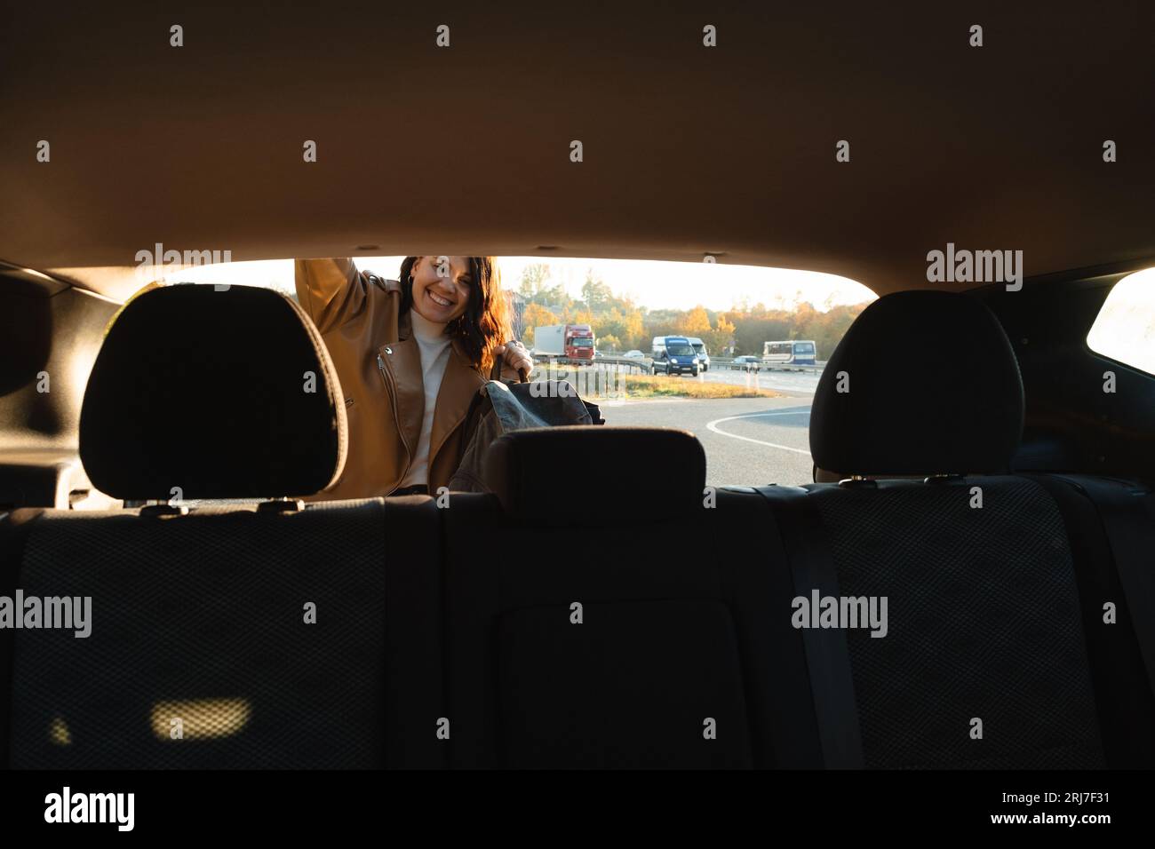 A woman smiles as she takes things out of the trunk of her car, viewed ...