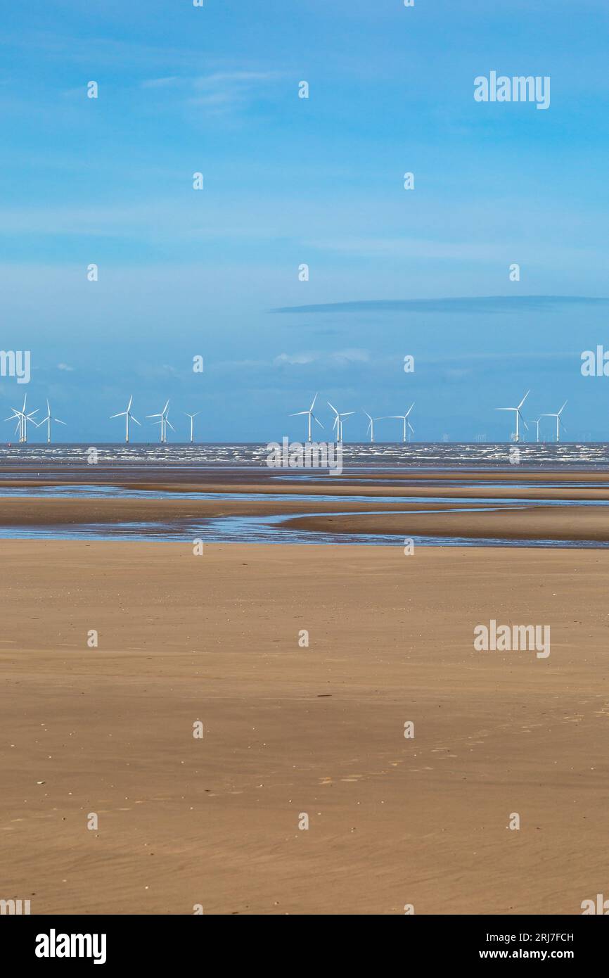 A view over a sandy beach at low tide with an off shore wind farm in ...