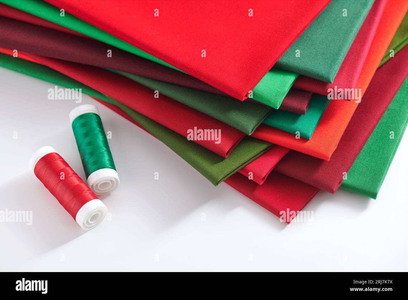 Pile of red and green fabrics and spools of thread on white background ...