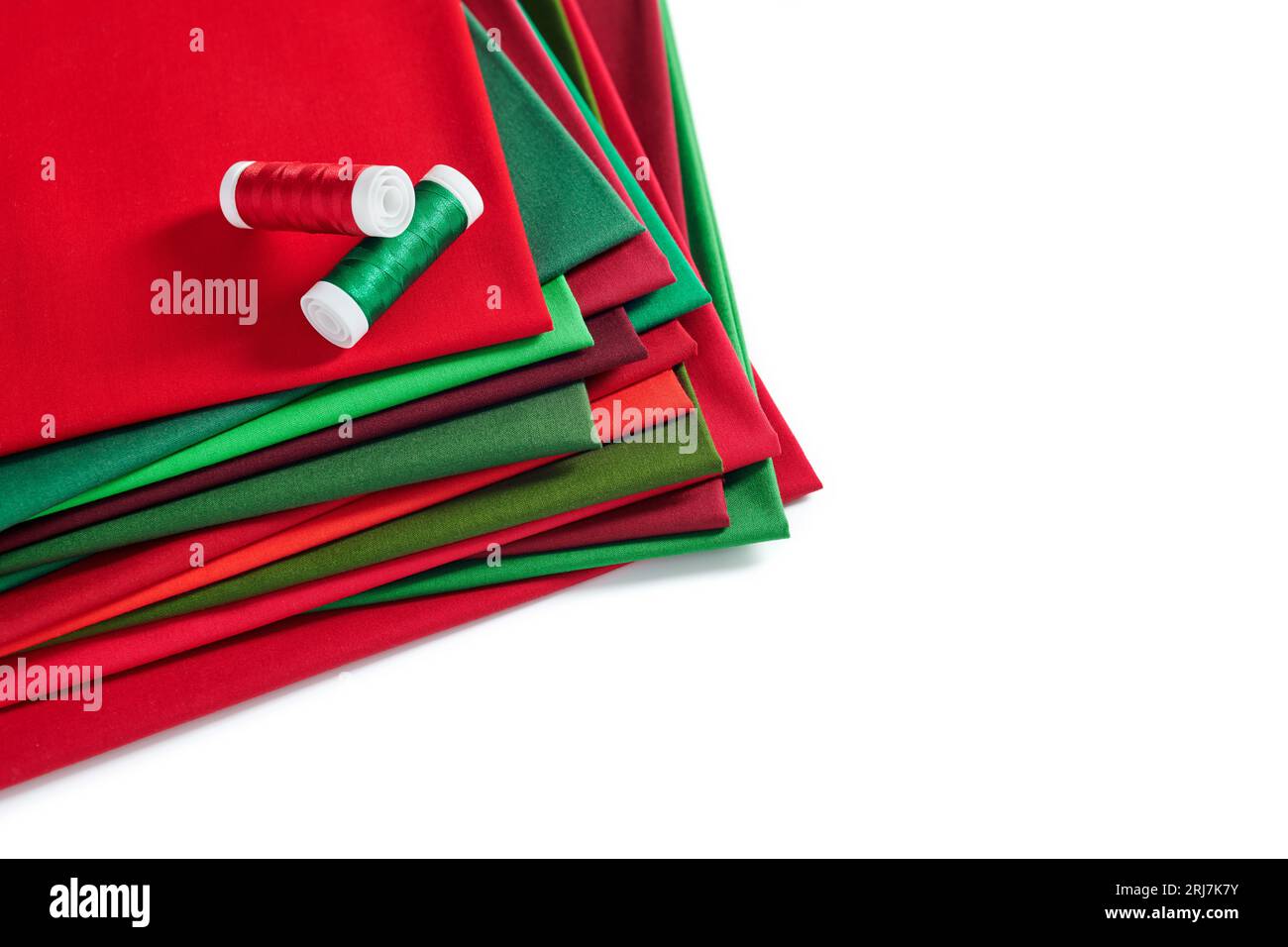 Pile of red and green fabrics and spools of thread on white background ...