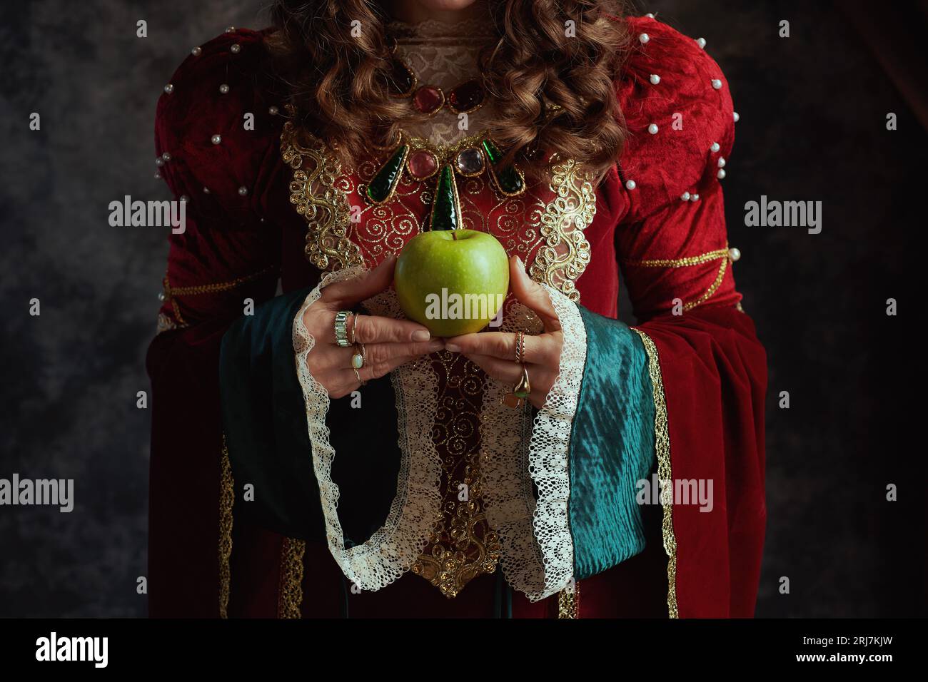 Closeup on medieval queen in red dress with green apple on dark gray ...