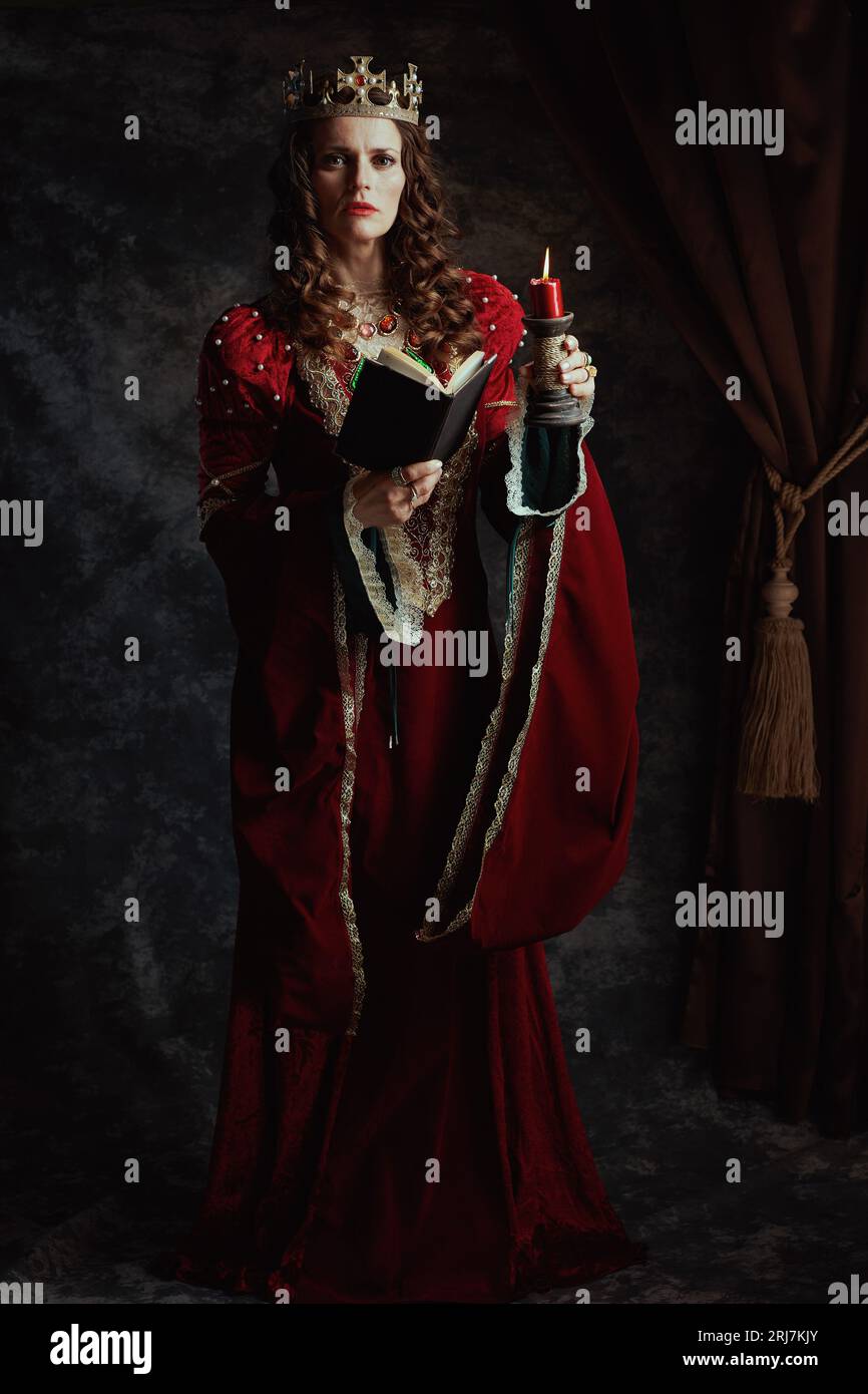 Full length portrait of medieval queen in red dress with book, candle ...