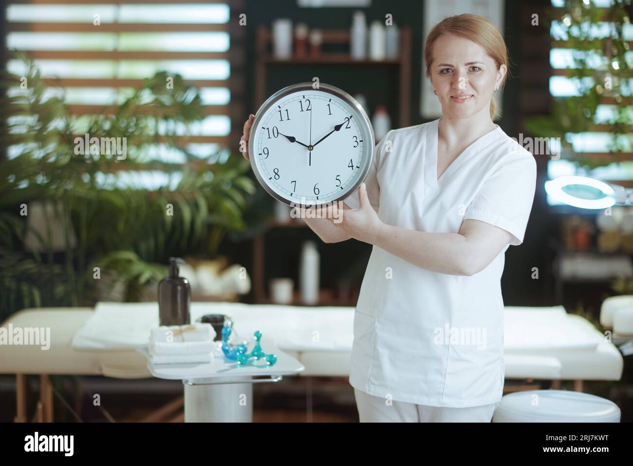Healthcare time. female massage therapist in spa salon with clock Stock ...