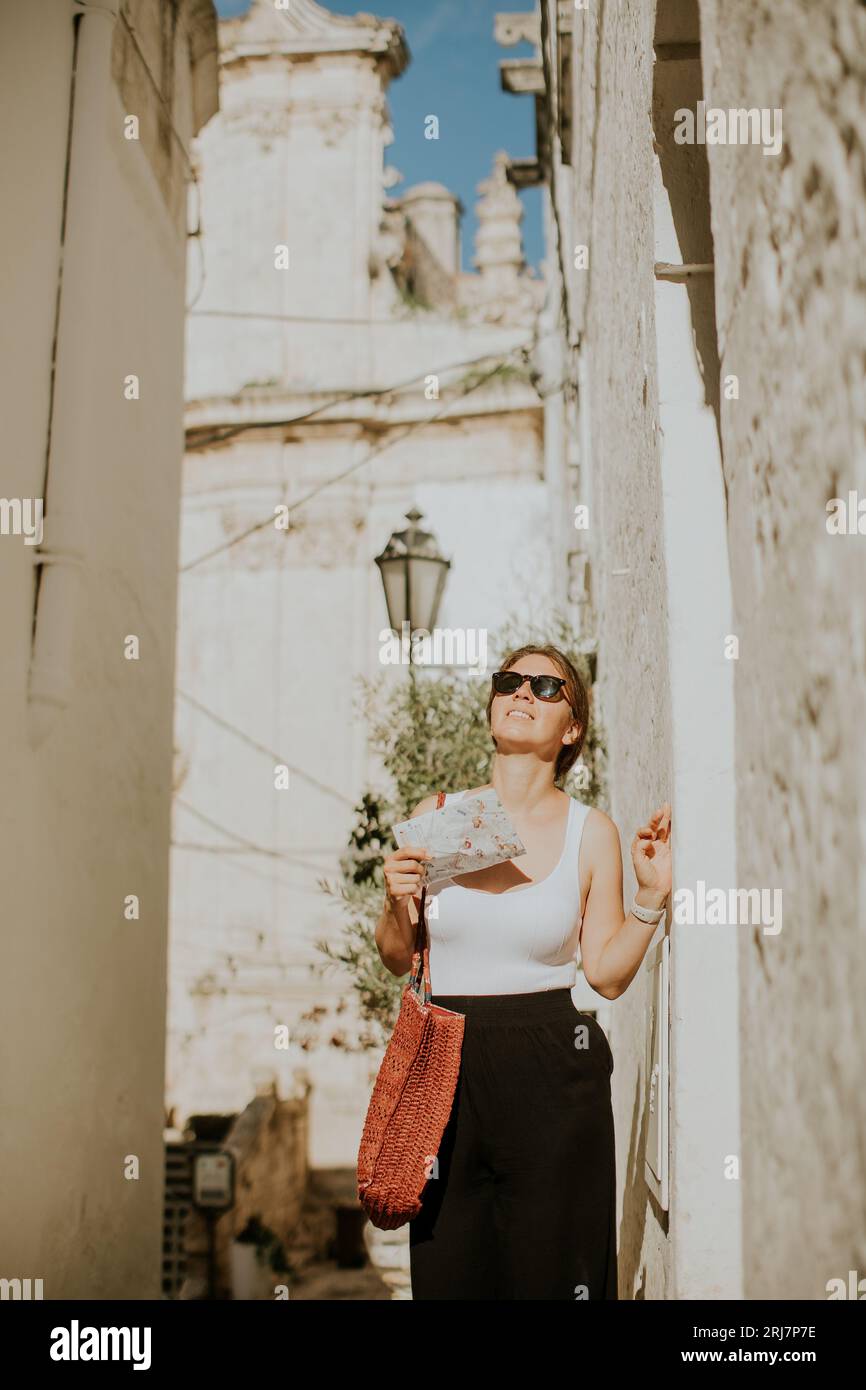 Female tourist with a paper city map on narrow streets of Ostuni, Italy ...