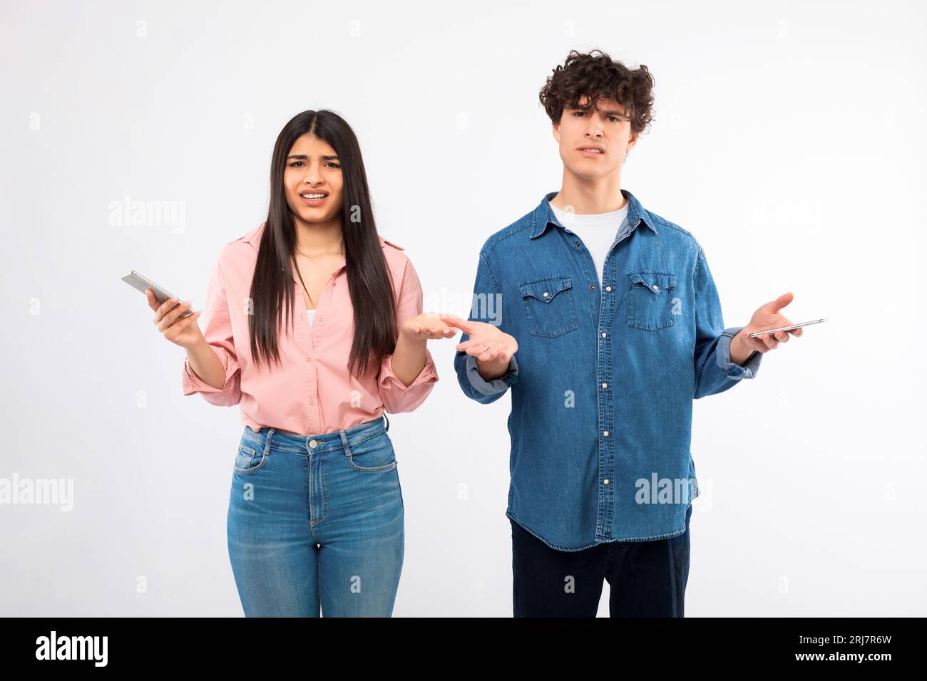 Discontented Young Couple Holding Mobile Phones Over White Studio ...