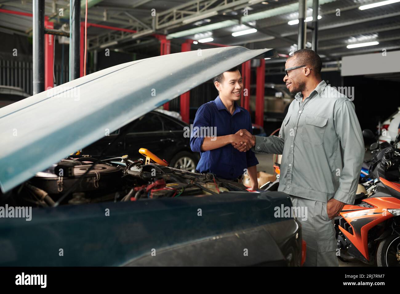 Happy car owner shaking hand of mechanic after having engine swapped ...
