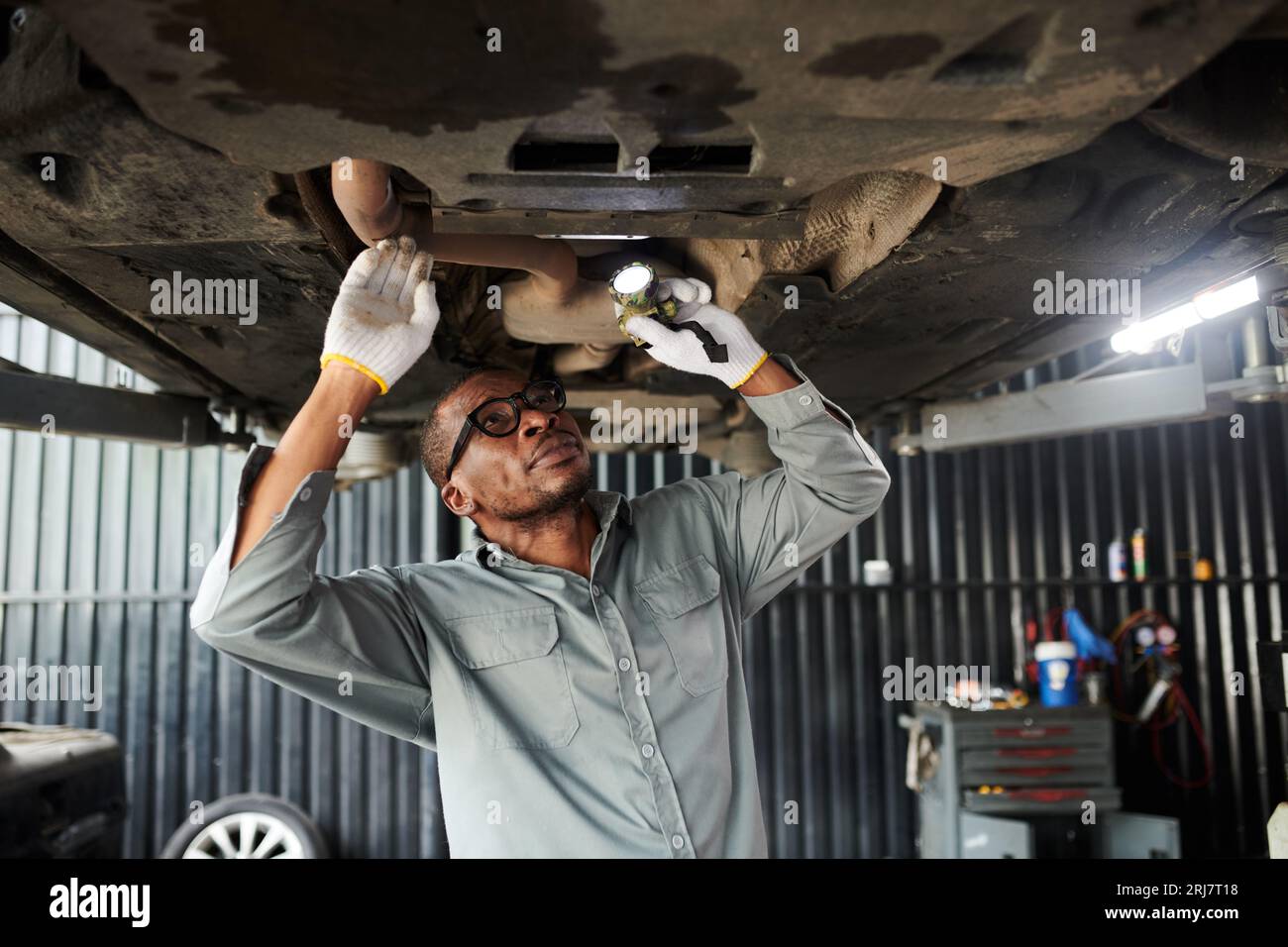 Mechanic with flashlight examining bottom of suspended car Stock Photo ...