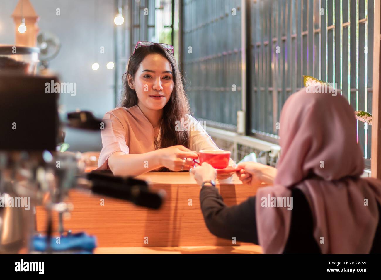 A beautiful Asian barista handing a cup of coffee to customers who wait ...