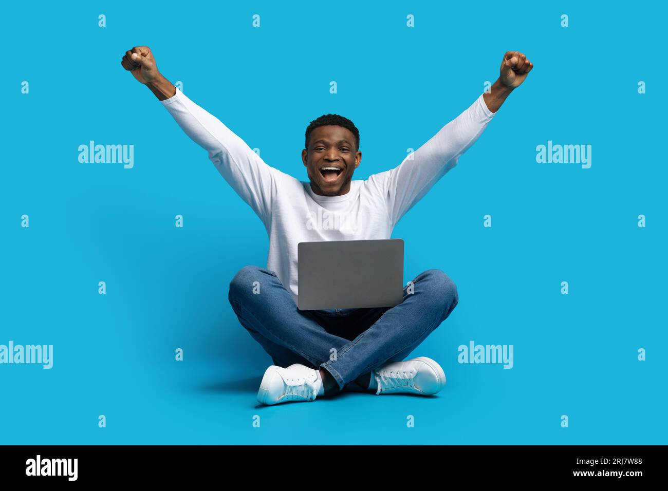 Emotional young black man using computer laptop, raising hands up Stock Photo - Alamy