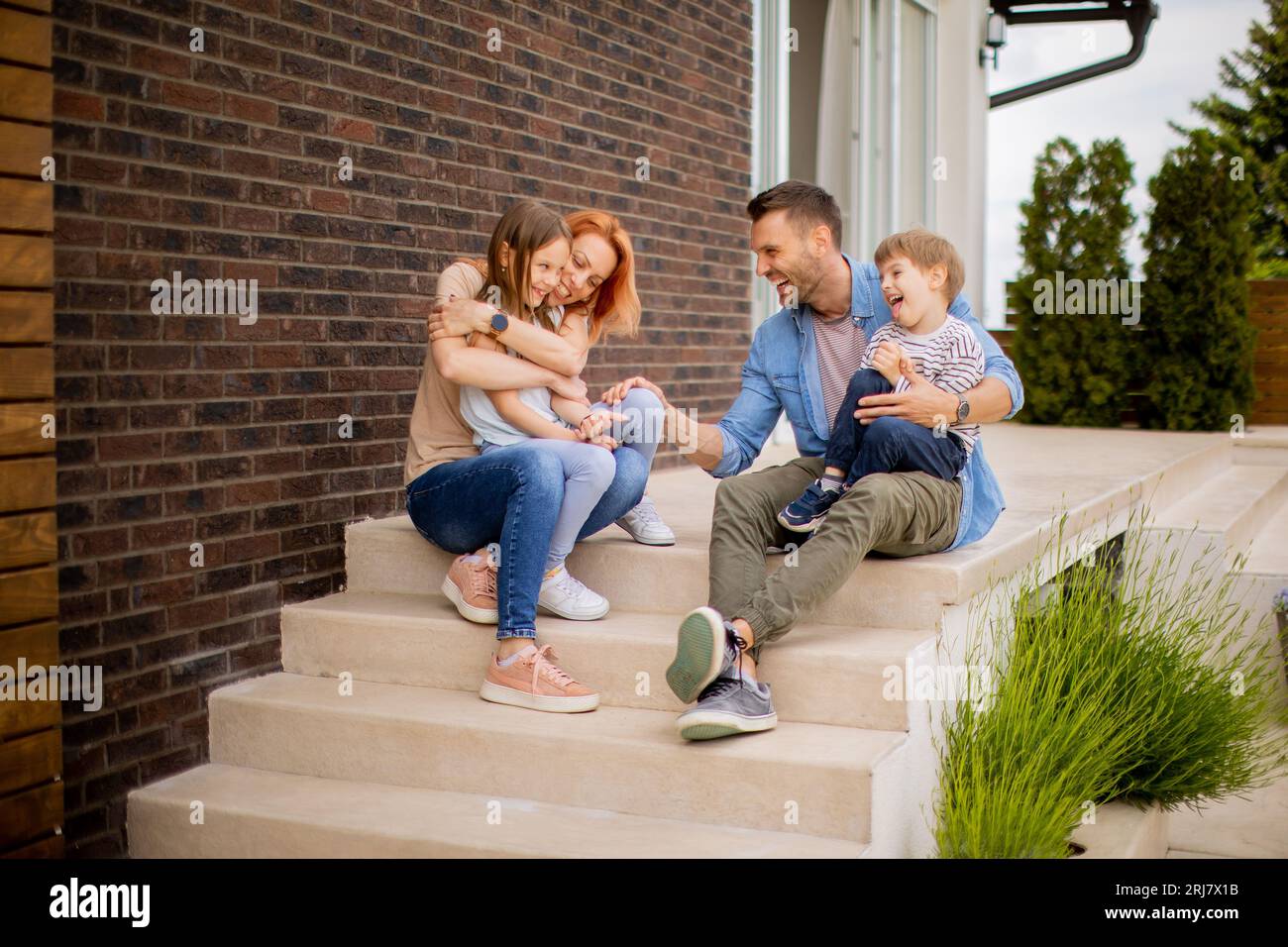 Family with a mother, father, son and daughter sitting outside on steps ...